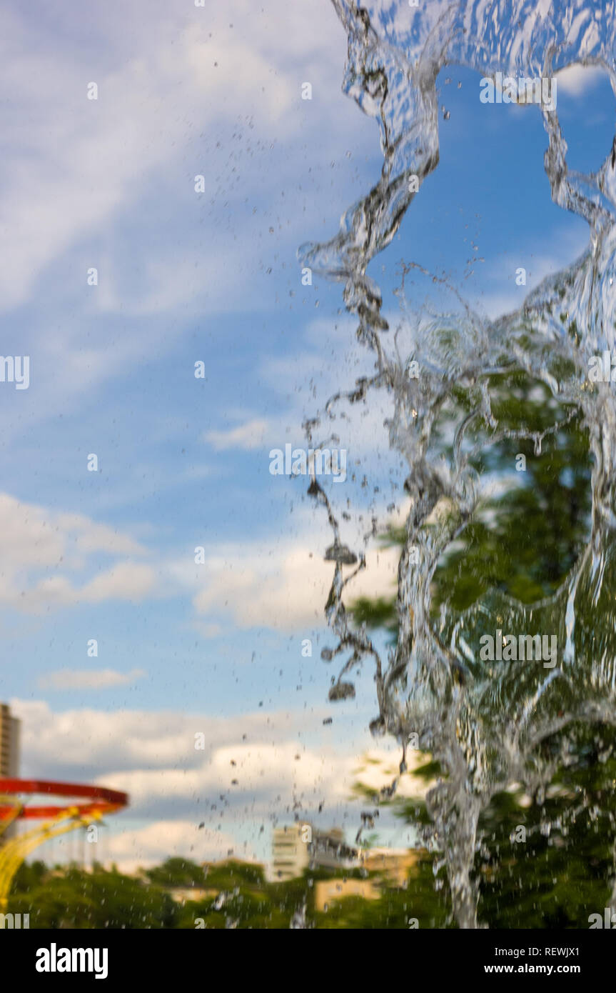 transparent falling water vertical flows against a blue sky and green ...