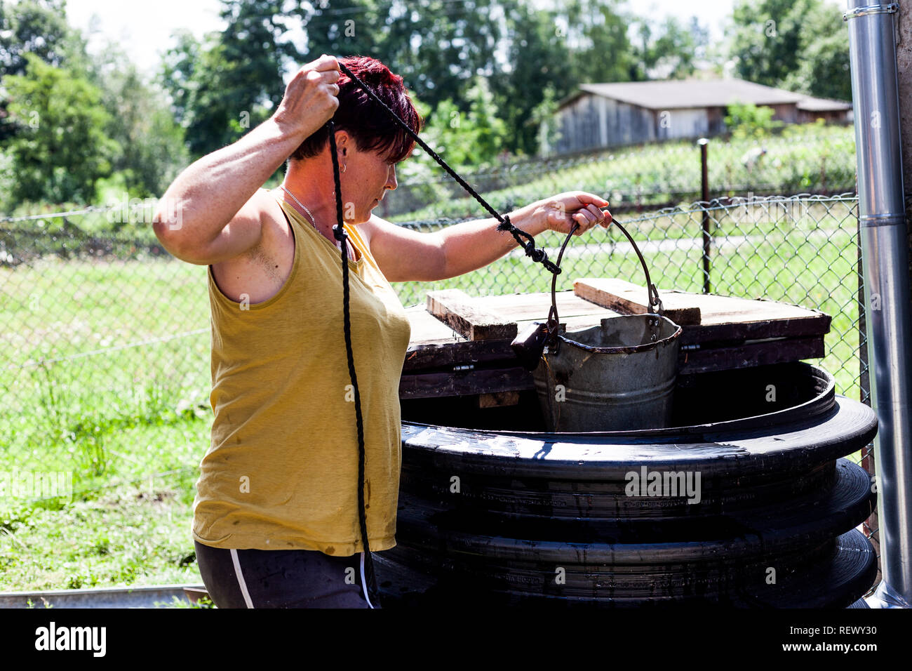 Side view of a hardworking mother holding a metal bucket. The woman ...