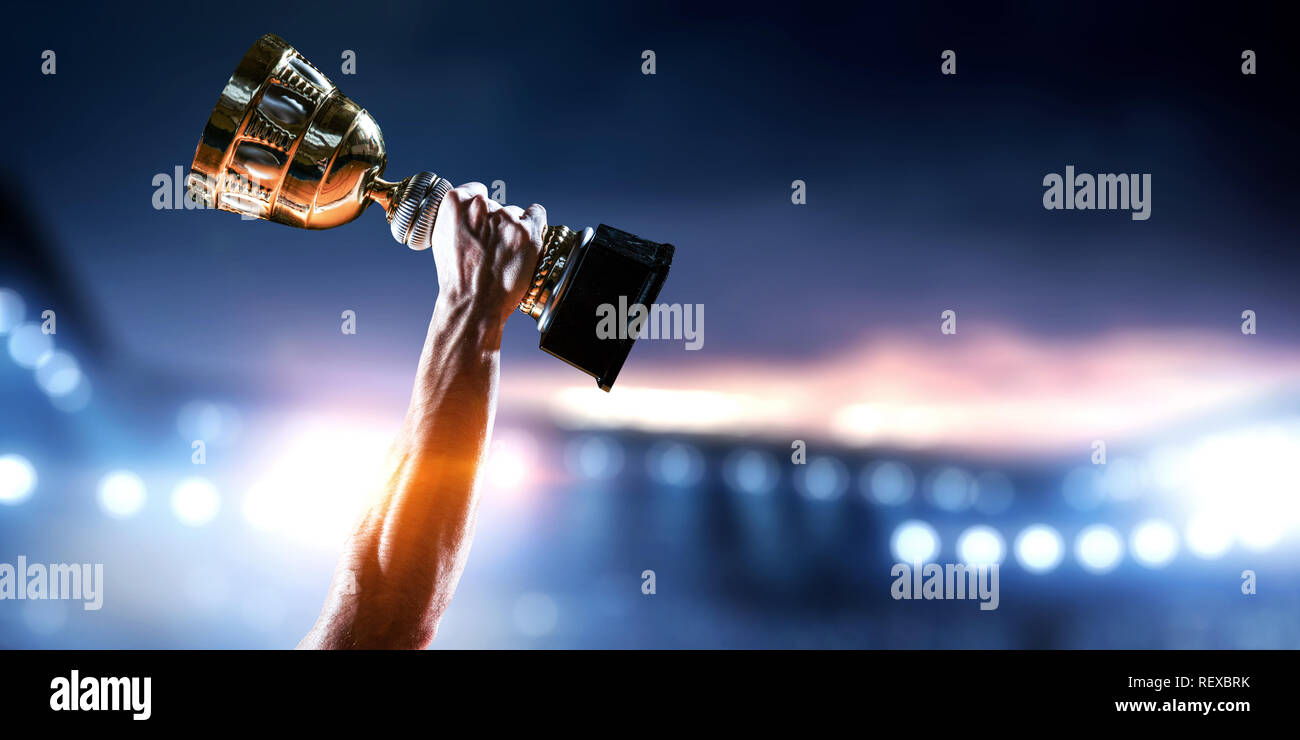 Hand of athlete holding cup trophy against stadium. Mixed media Stock ...