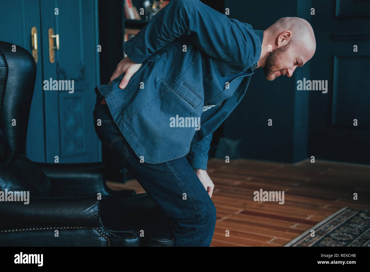 The attractive bald bearded man is holding onto his back, trying to get ... The attractive bald bearded man is holding onto his back, trying to get ...