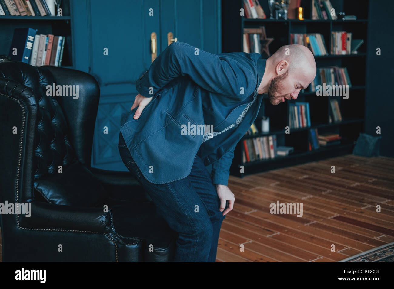 The attractive bald bearded man is holding onto his back, trying to get ...