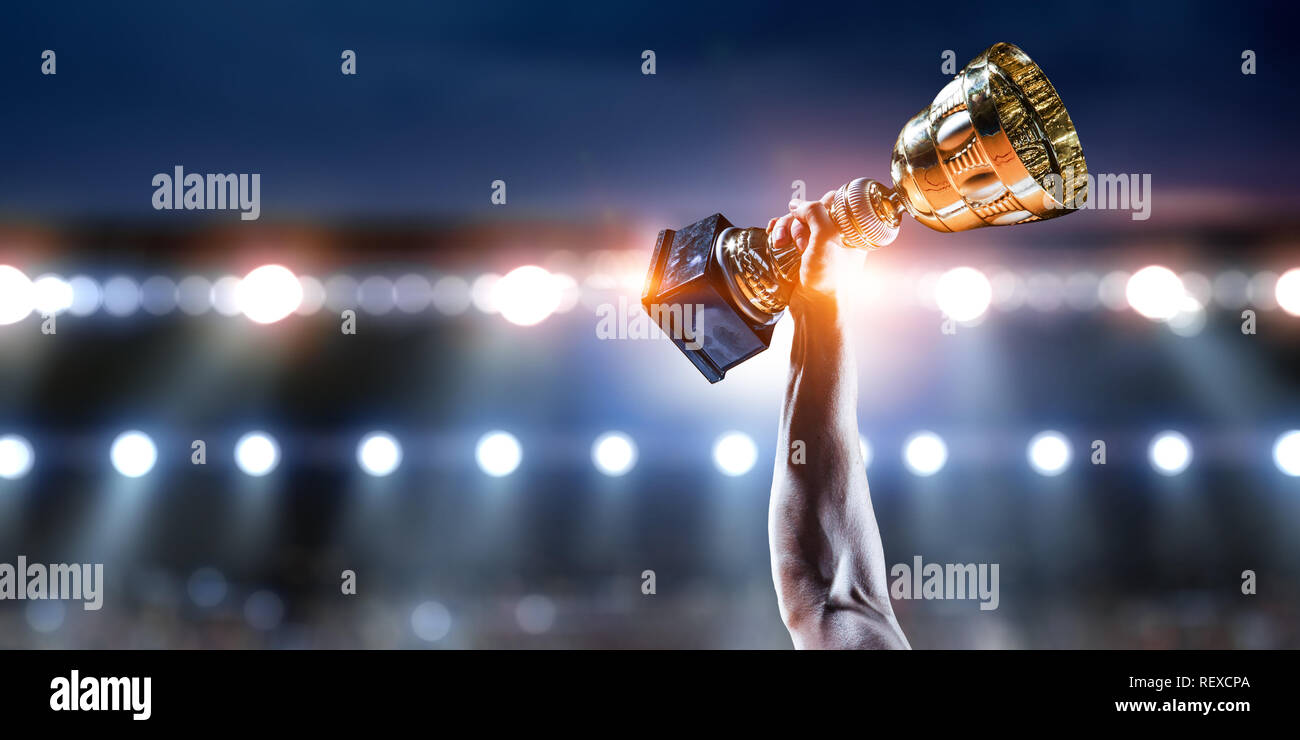 Hand of athlete holding cup trophy against stadium. Mixed media Stock ...