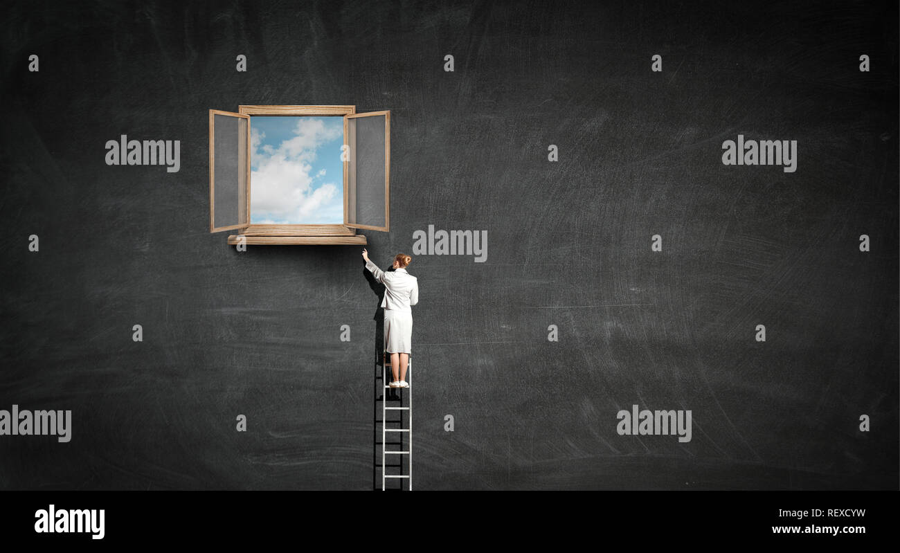Businesswoman standing on ladder and reaching up opened window in wall ...