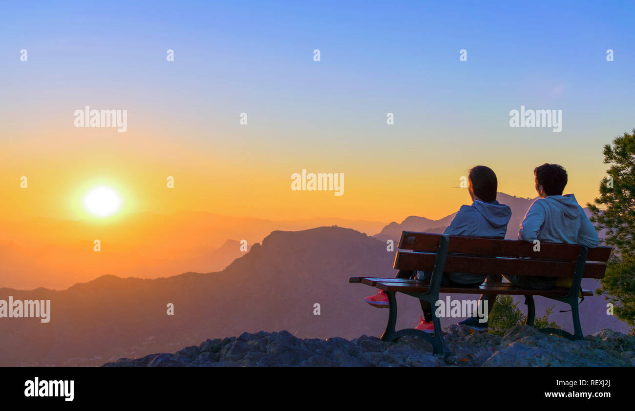 Romantic scene of a couple watching the sunrise in the top of a ...
