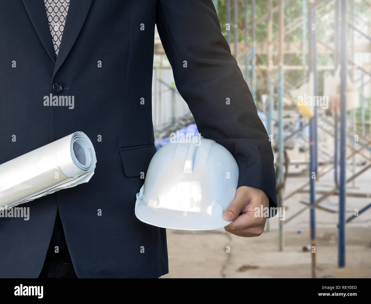 Engineer in suit with blueprint and helmet in construction site Stock ...