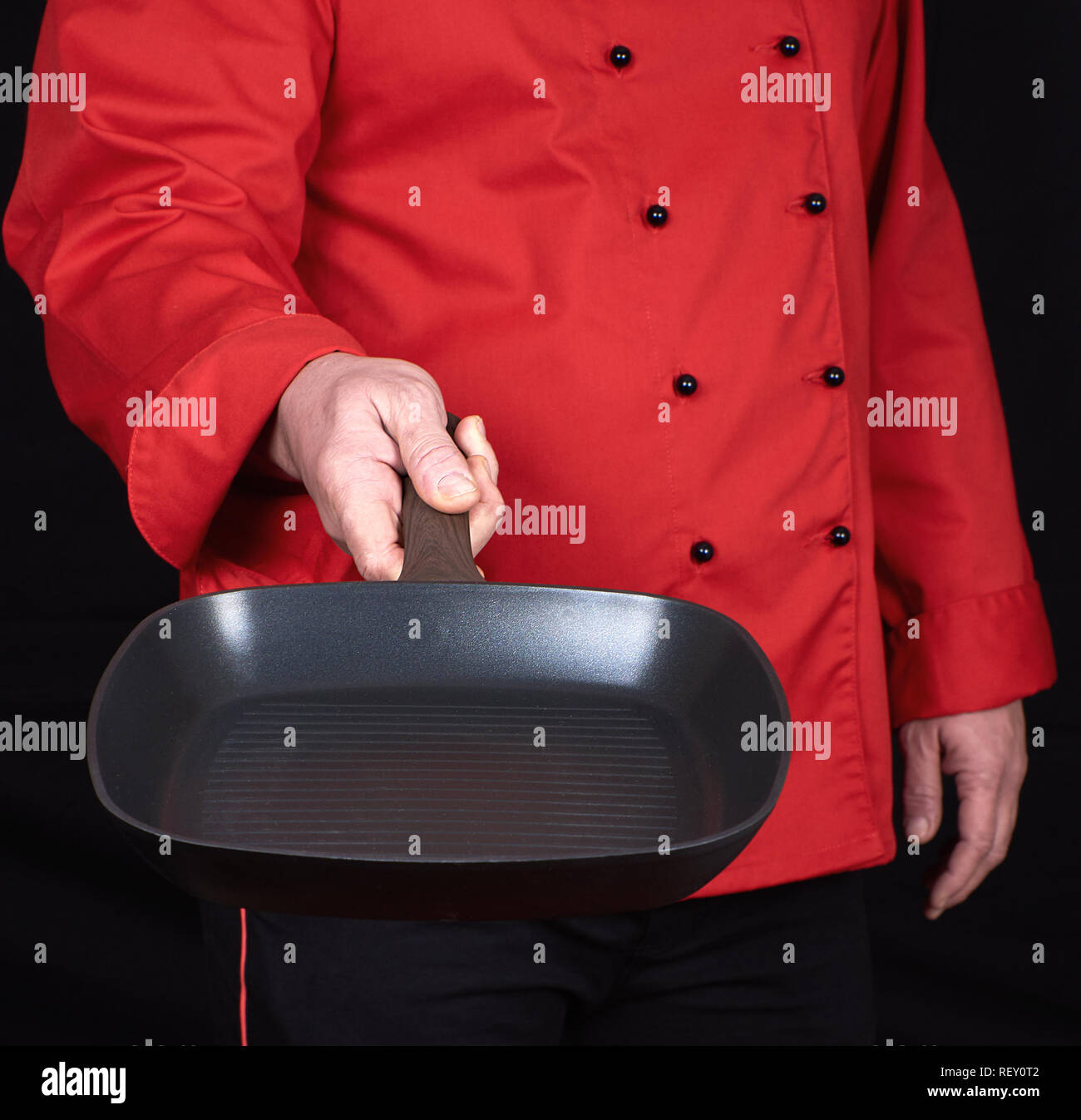 cook in red uniform holding an empty square black frying pan, black ...