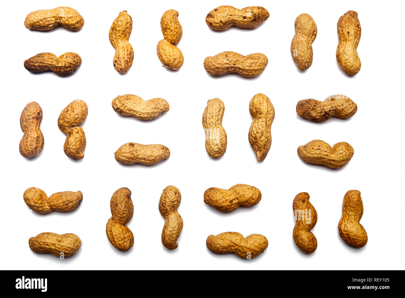 A collection of unpeeled peanuts lie in horizontal rows on an isolated ...