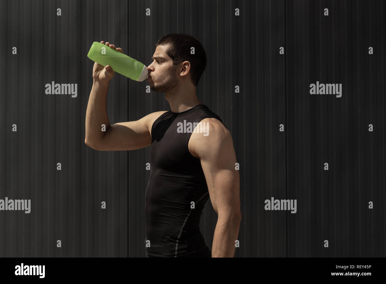 Sport model man drinking water from a plastic bottle on gray background ...
