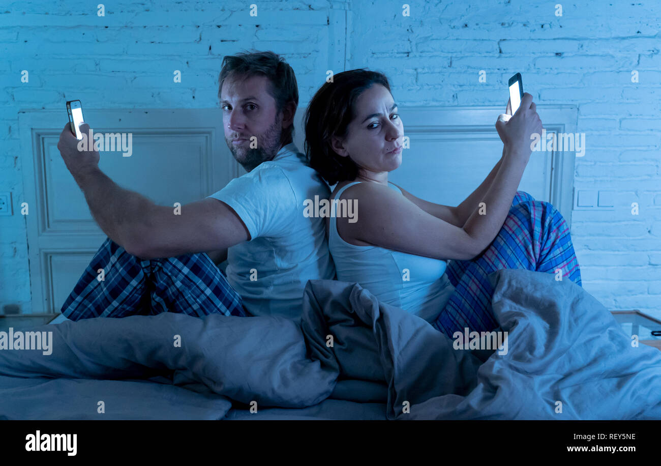Sad man and woman married couple using their smart mobile phone in bed ...
