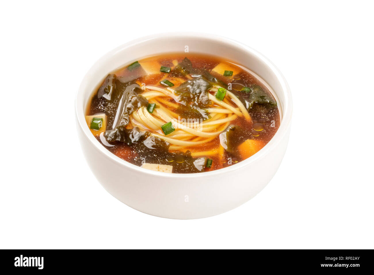 A photo of a bowl of miso soup with tofu, scallions, noodles, and wakame seaweed, isolated on a ...