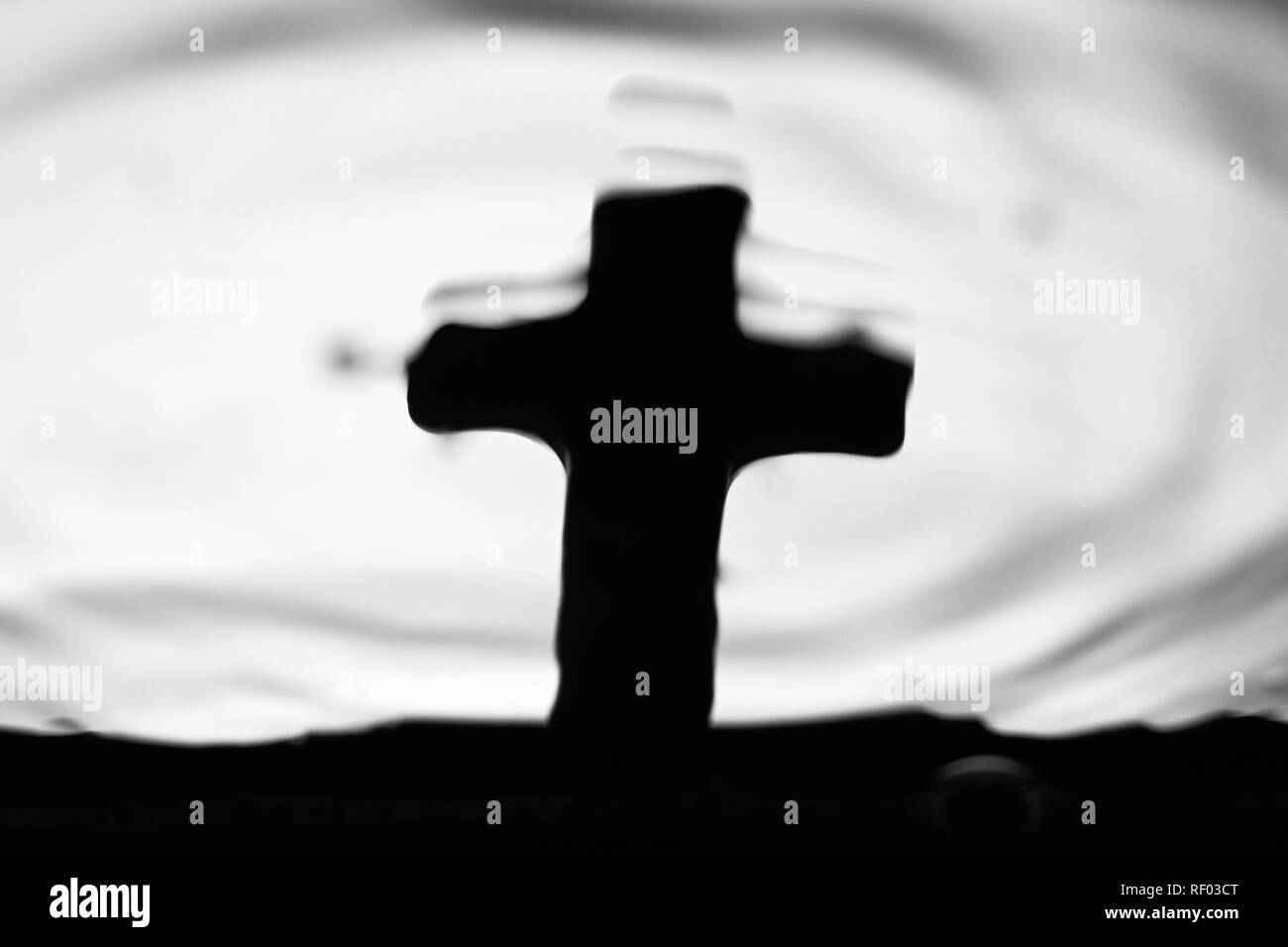 Gravestone cross reflected in rippling water in an atmospheric ...