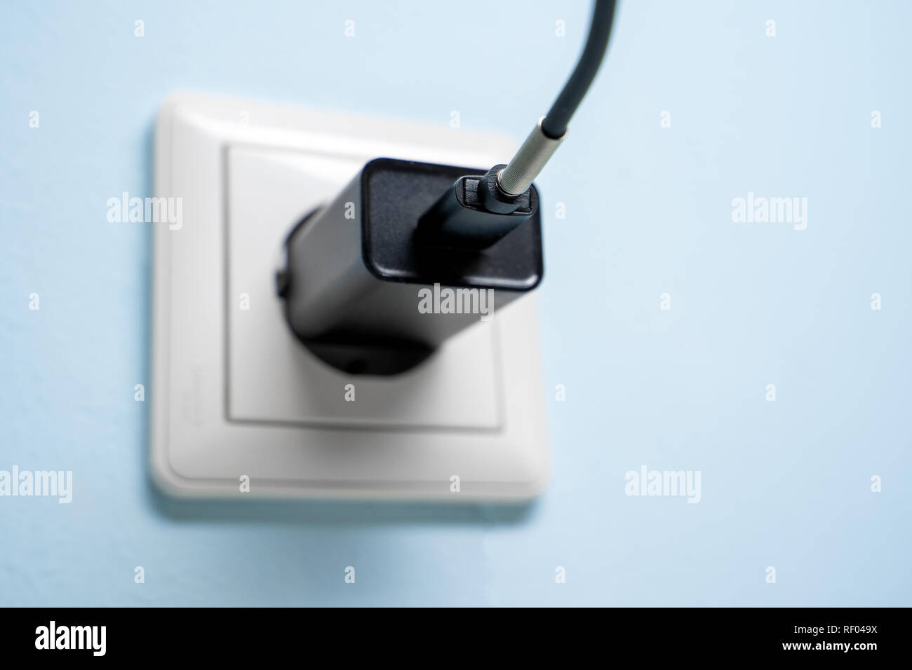 Photo of charger in socket on background of blue wall Stock Photo - Alamy