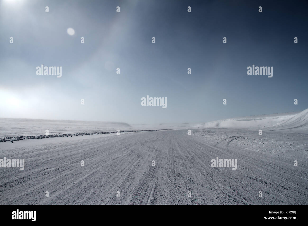 An ice road leading towards snow covered hills with a partial sundog ...