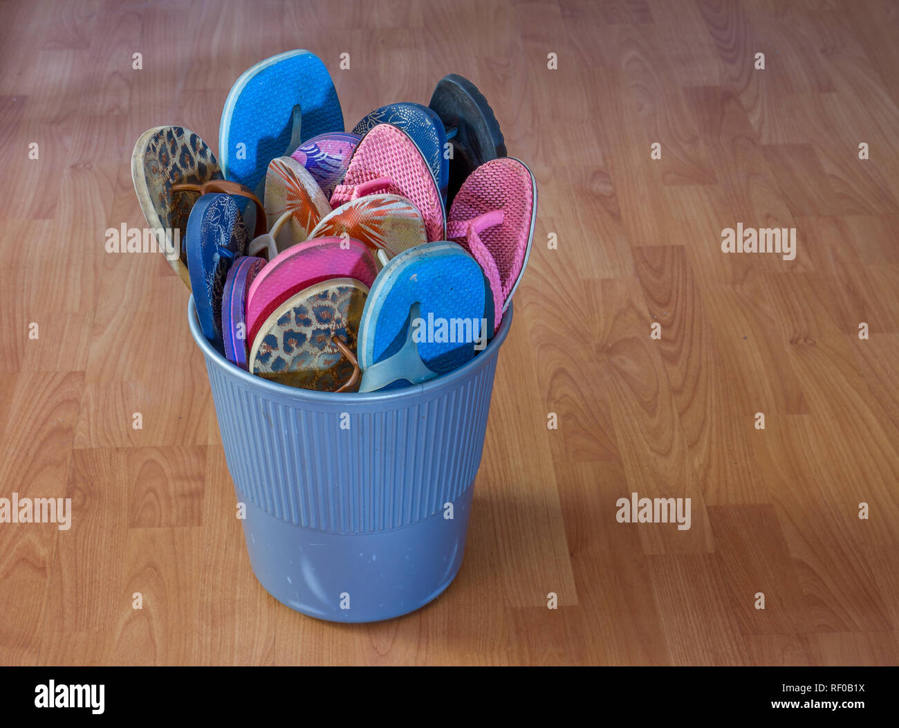 Pairs of colorful slip slops stored in a plastic bucket at the end of ...