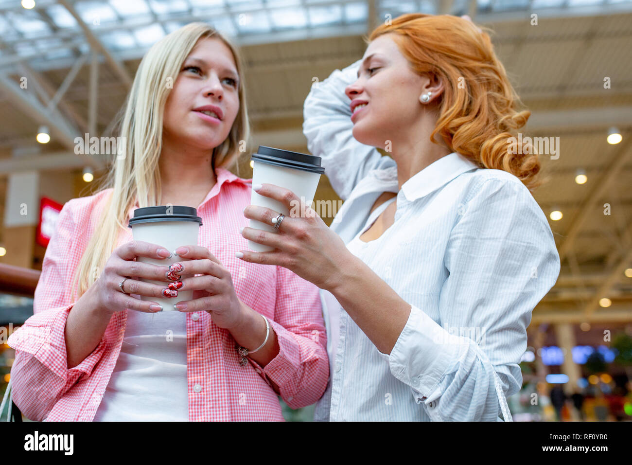 Two beautiful smiling women with disposable coffee cups talking in ...