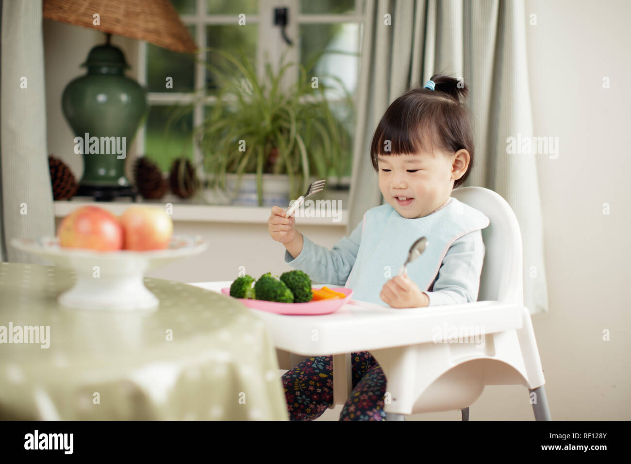toddler girl eating healthy vegetable sitting on high chair beside a ...
