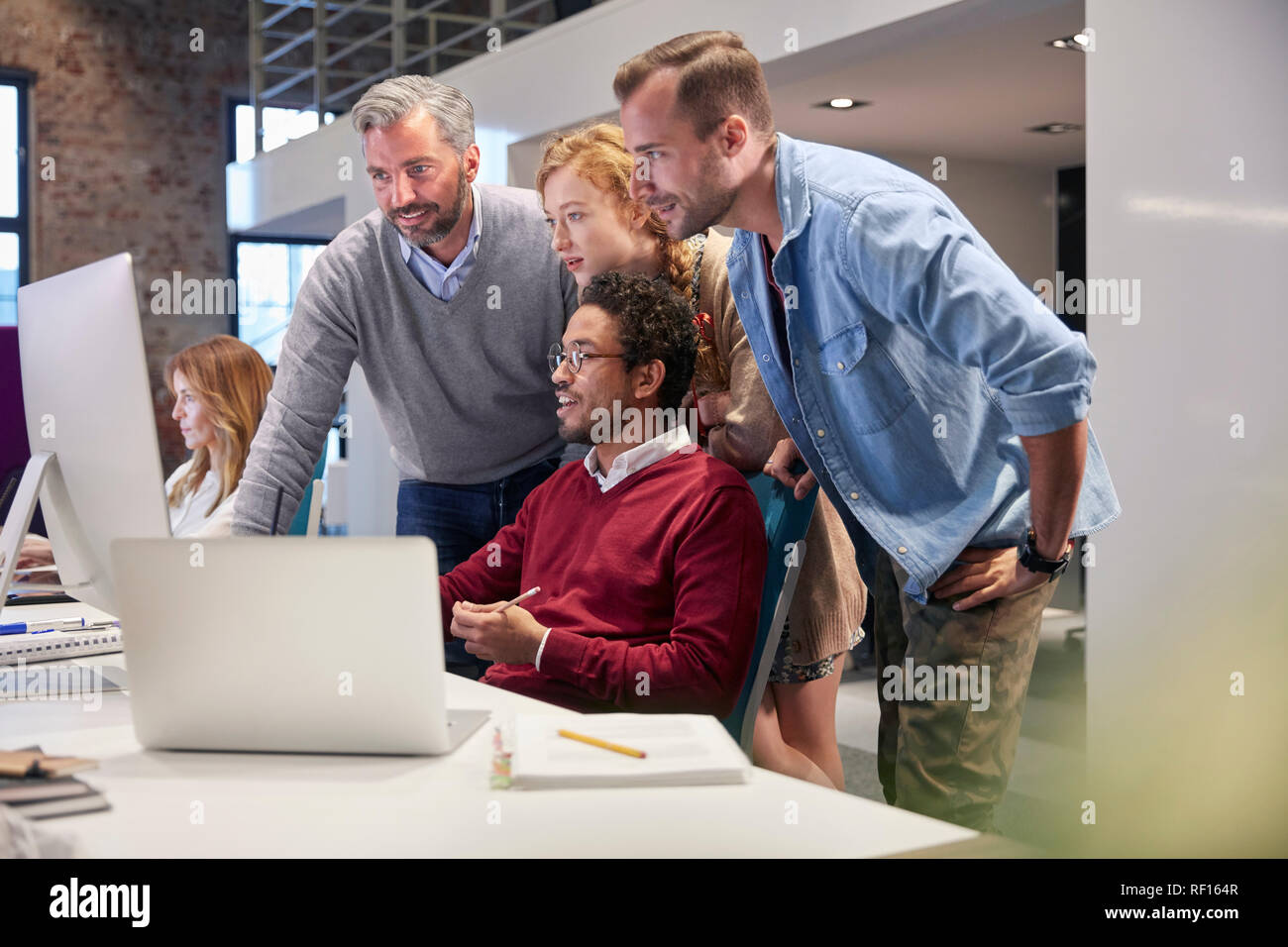 Colleagues looking over shoulder of young man working in modern office ...