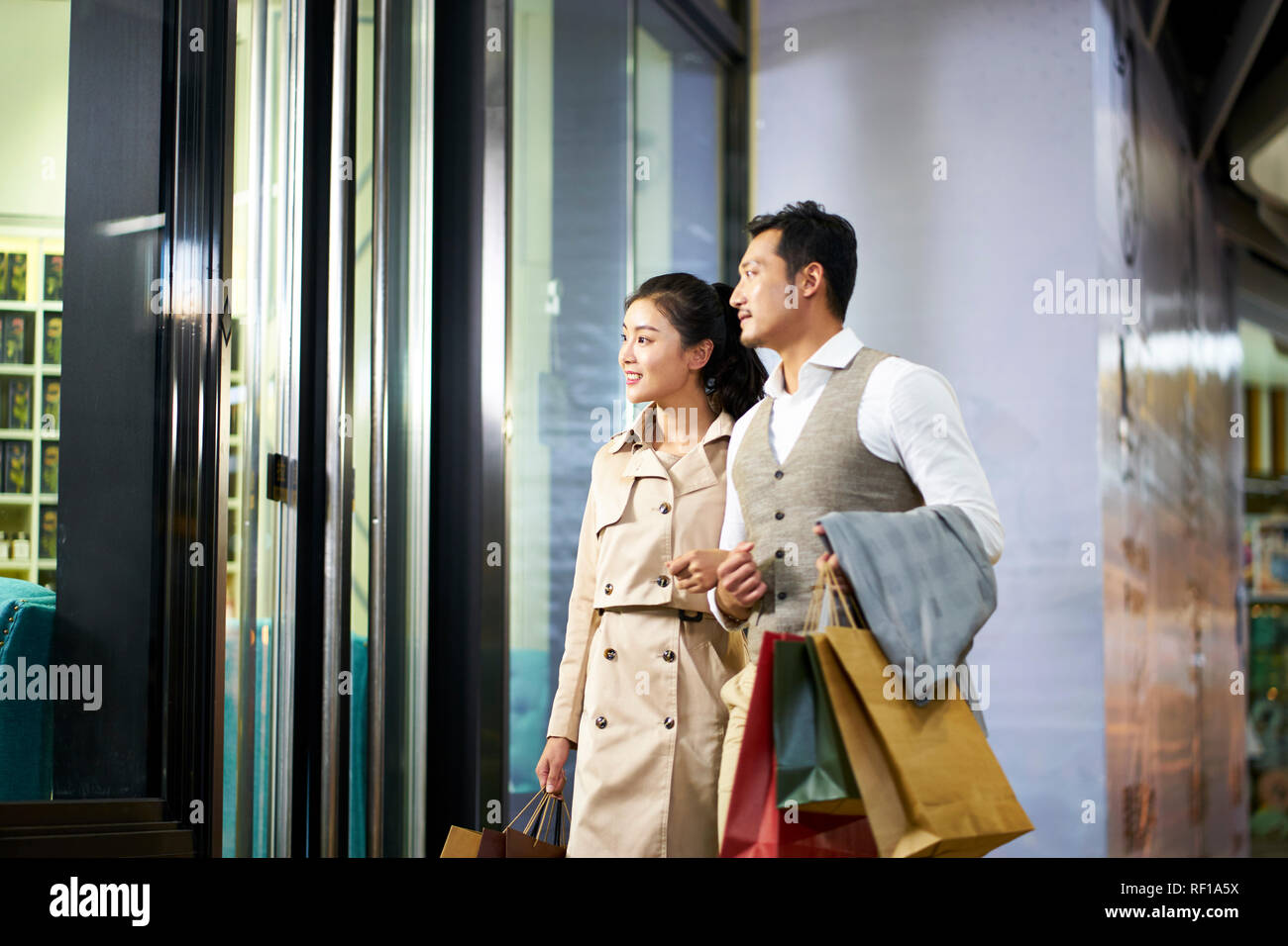 happy young asian couple looking into window of a shop in shopping mall ...