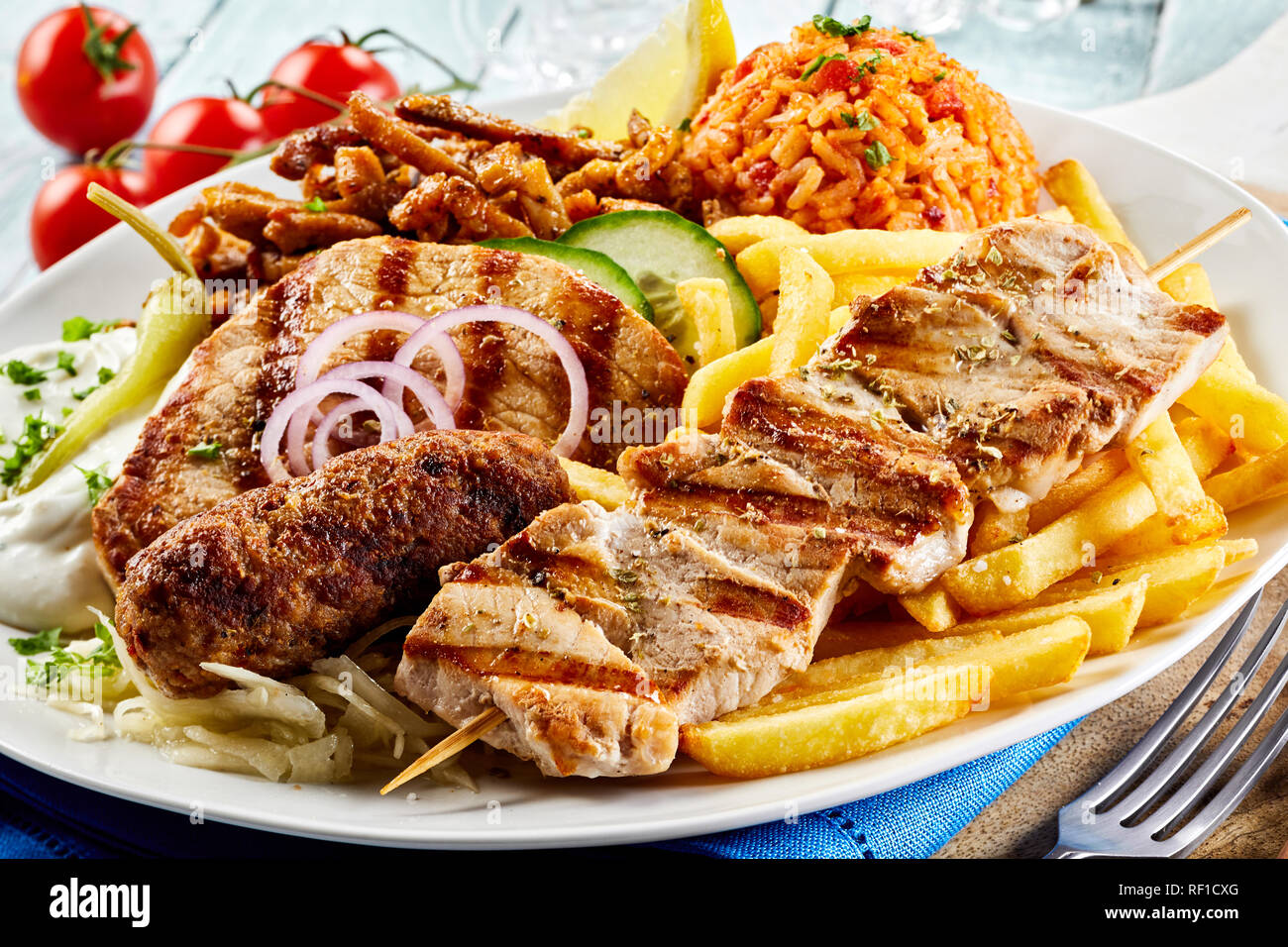Greek grill plate with assorted meats, crispy potato chips, tomato rice ...