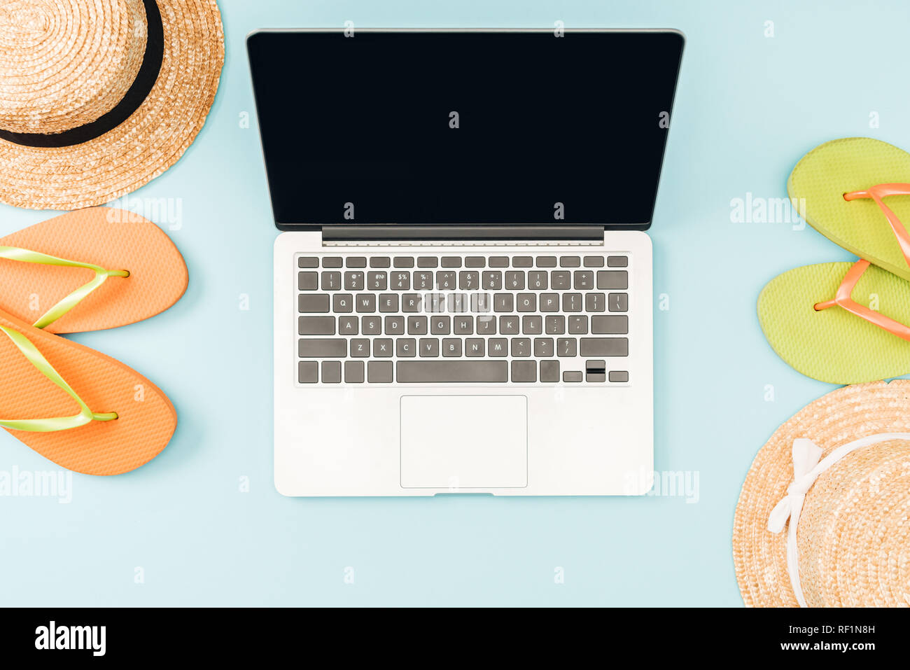 top view of laptop with blank screen near flip flops and straw hats on ...