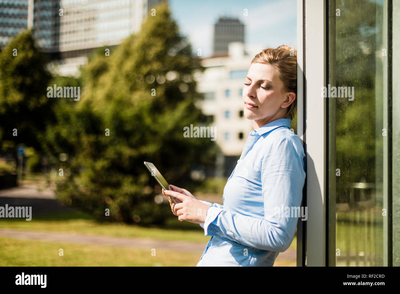 Woman leaning against a building holding tablet Stock Photo - Alamy