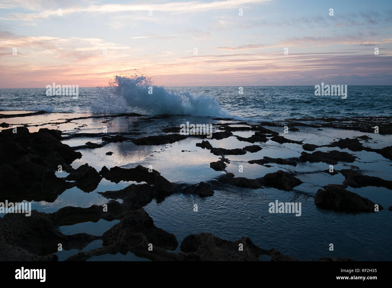 Splash of ocean waves against a background of sunset and rocks Stock ...