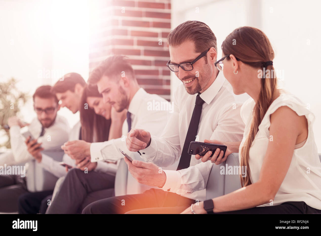 employees of the company using their smartphones sitting in the office ...