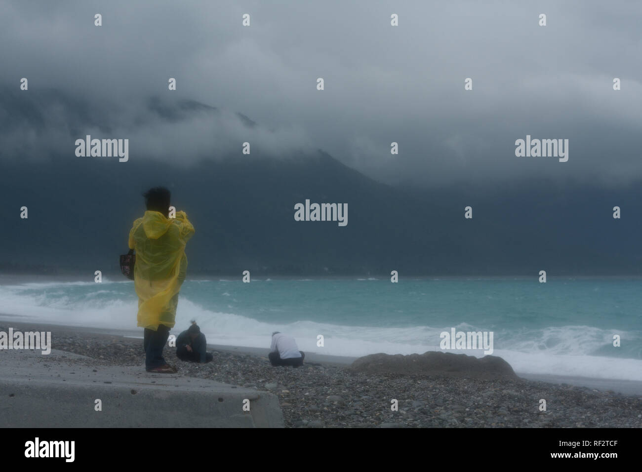 Woman in raincoat taking photos in rainy, windy weather, azure waters ...