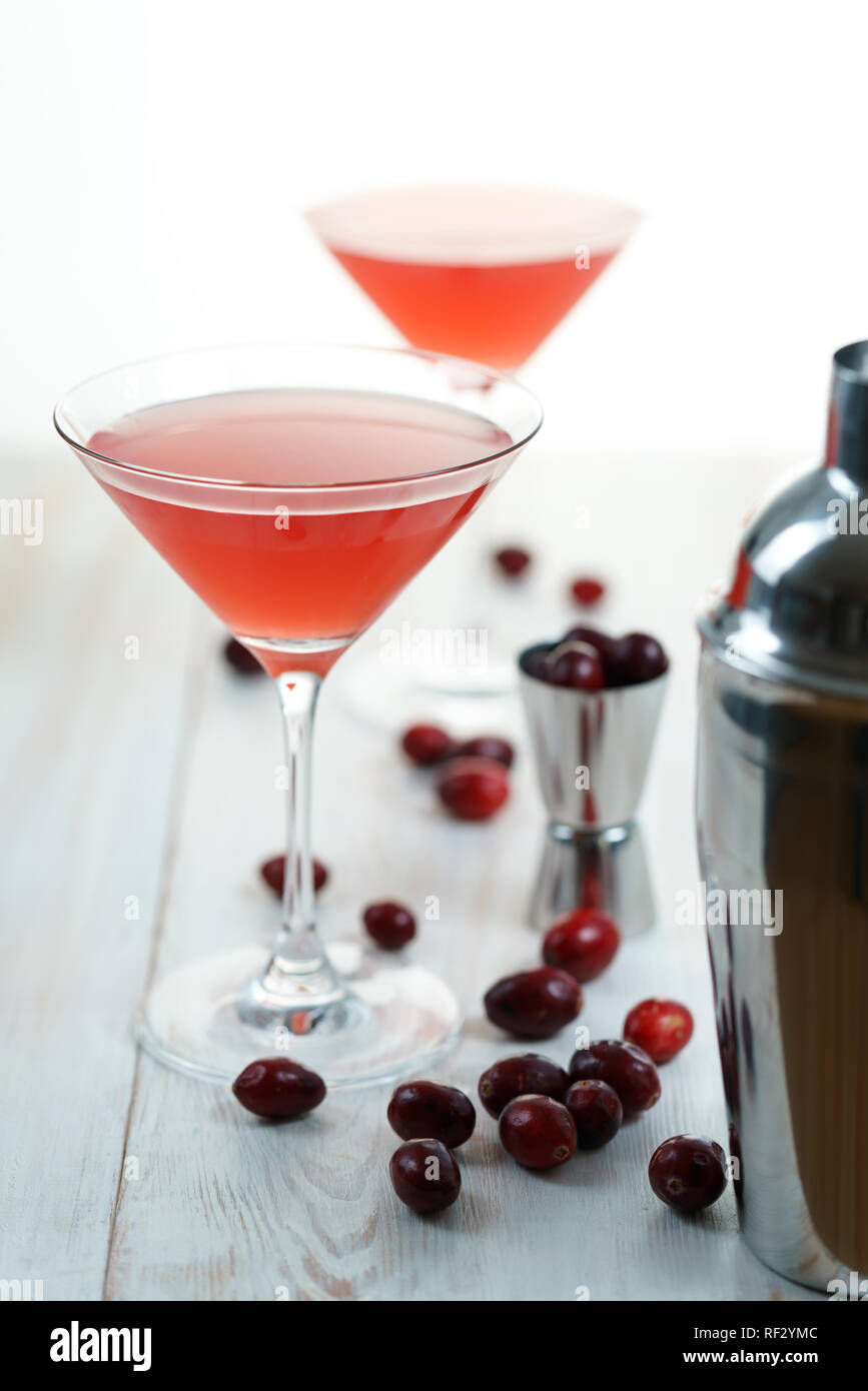 Cosmopolitan cocktail with cranberries, shaker and jigger. White wooden ...