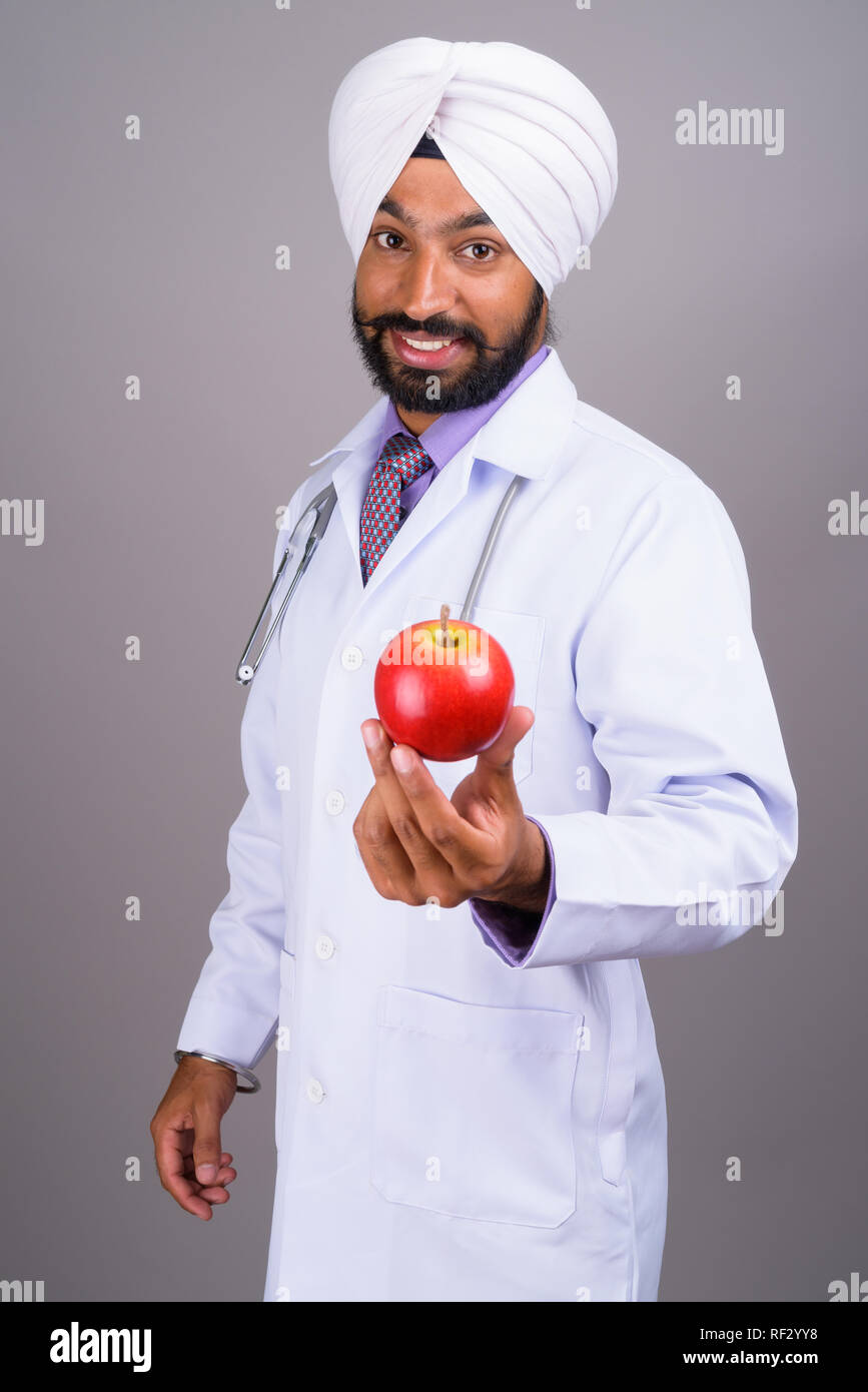 Young Indian Sikh man doctor smiling and holding apple Stock Photo - Alamy