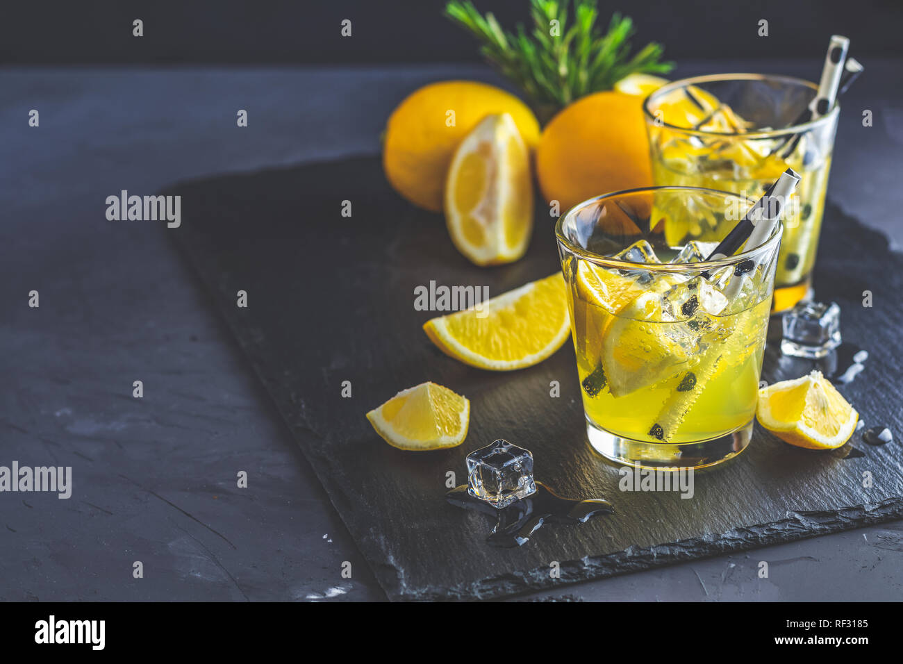 Lemon alcohol drink cocktail with ice, lemon and rosemary herb on black ...