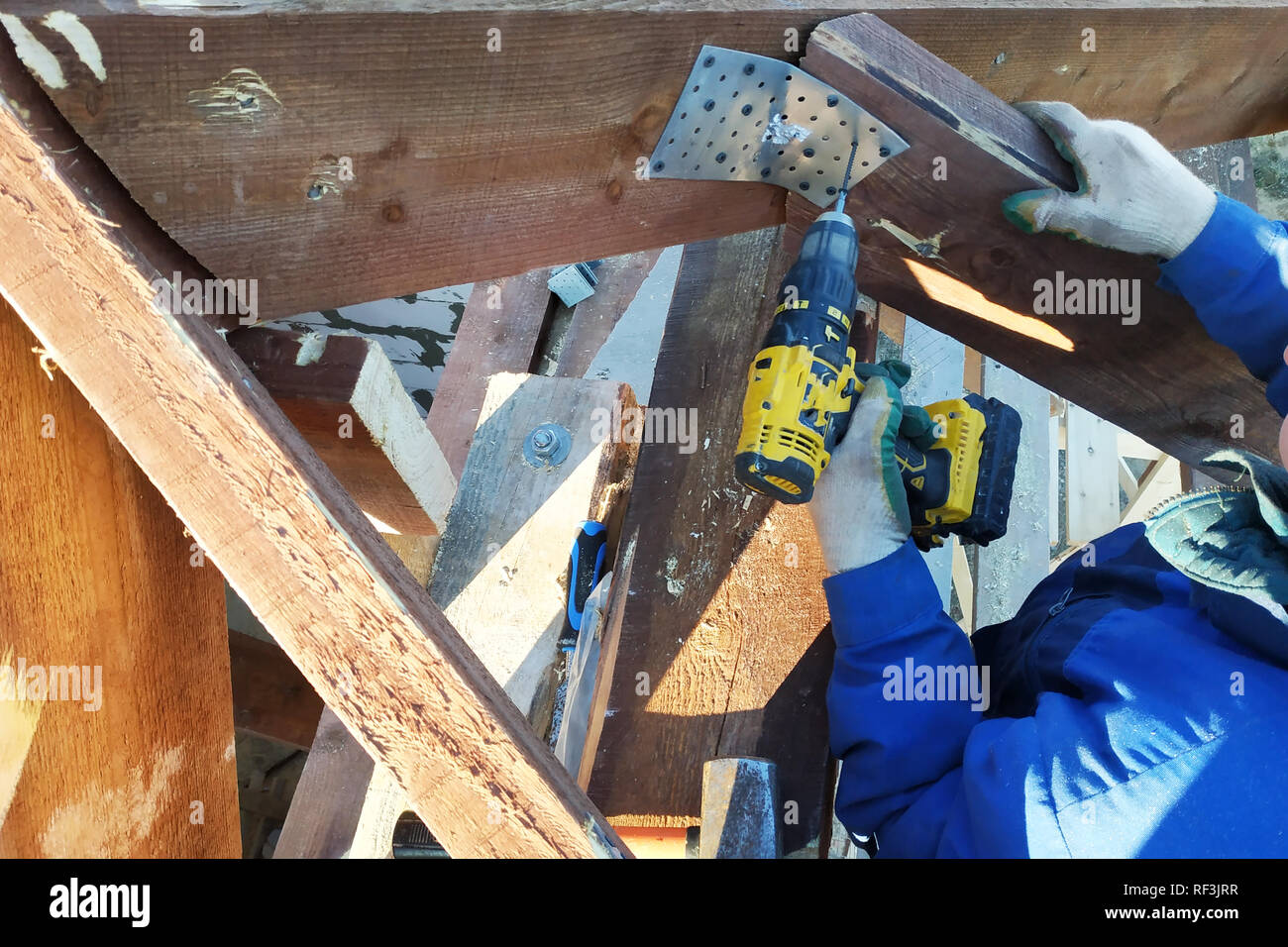 In a rafter of a roof the worker twists screws in a plate for screws ...