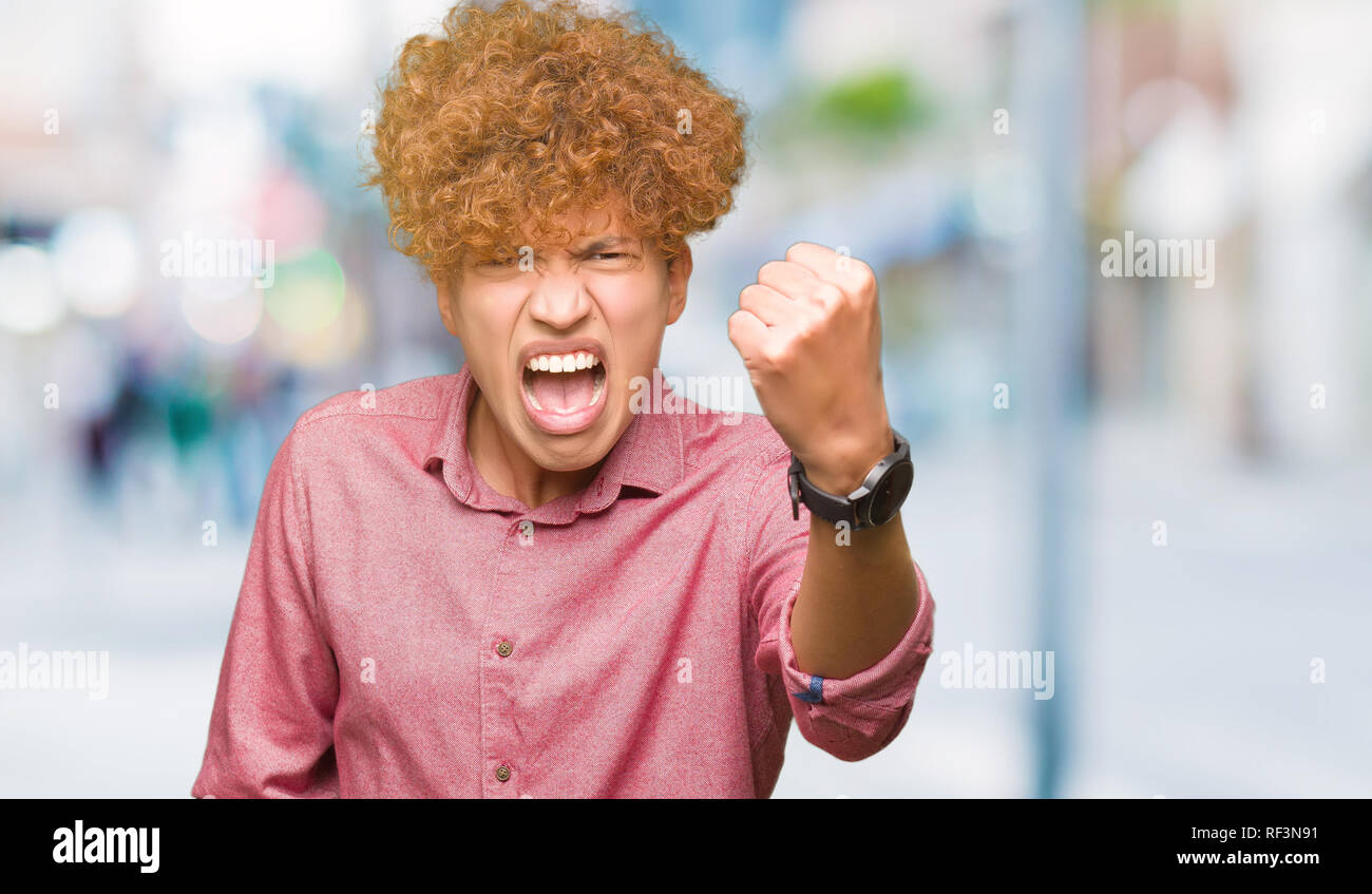 Young handsome business man with afro hair angry and mad raising fist ...
