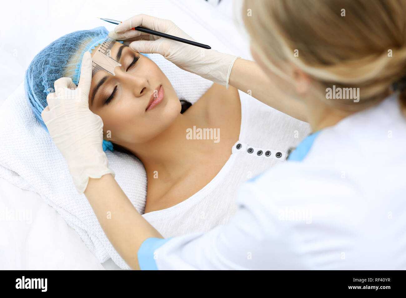 Professional beautician is going to correct eyebrow line at woman face ...