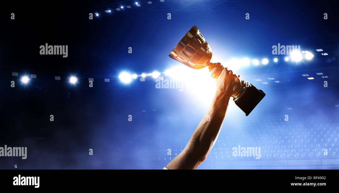 Hand of athlete holding cup trophy against stadium. Mixed media Stock ...
