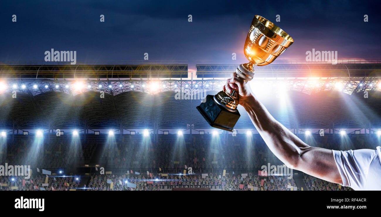 Hand of athlete holding cup trophy against stadium. Mixed media Stock ...