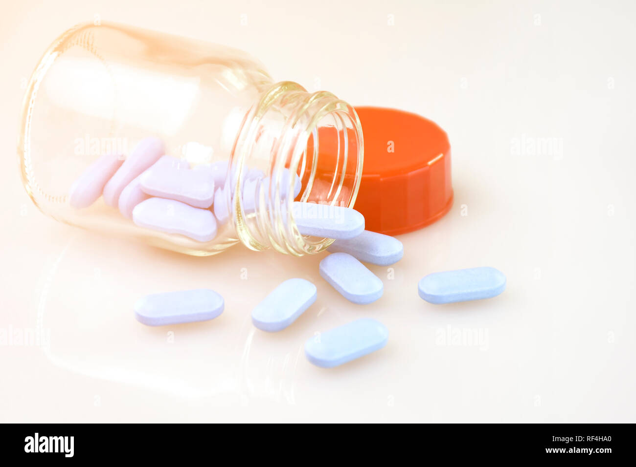 Blue caplets in glass bottle on white background wth warm light tone ...