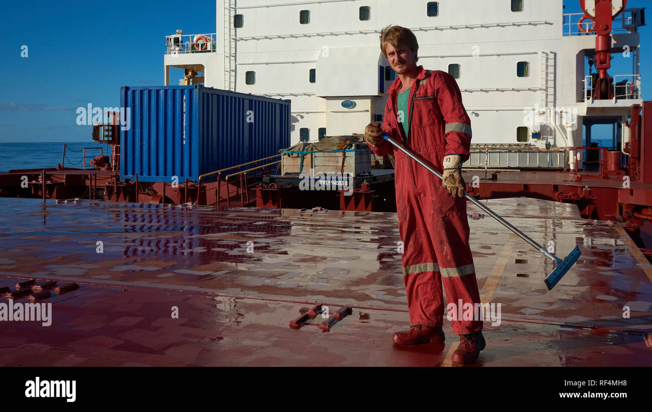 Ships crew members painting hatch cover outdoors with bright blue sky ...