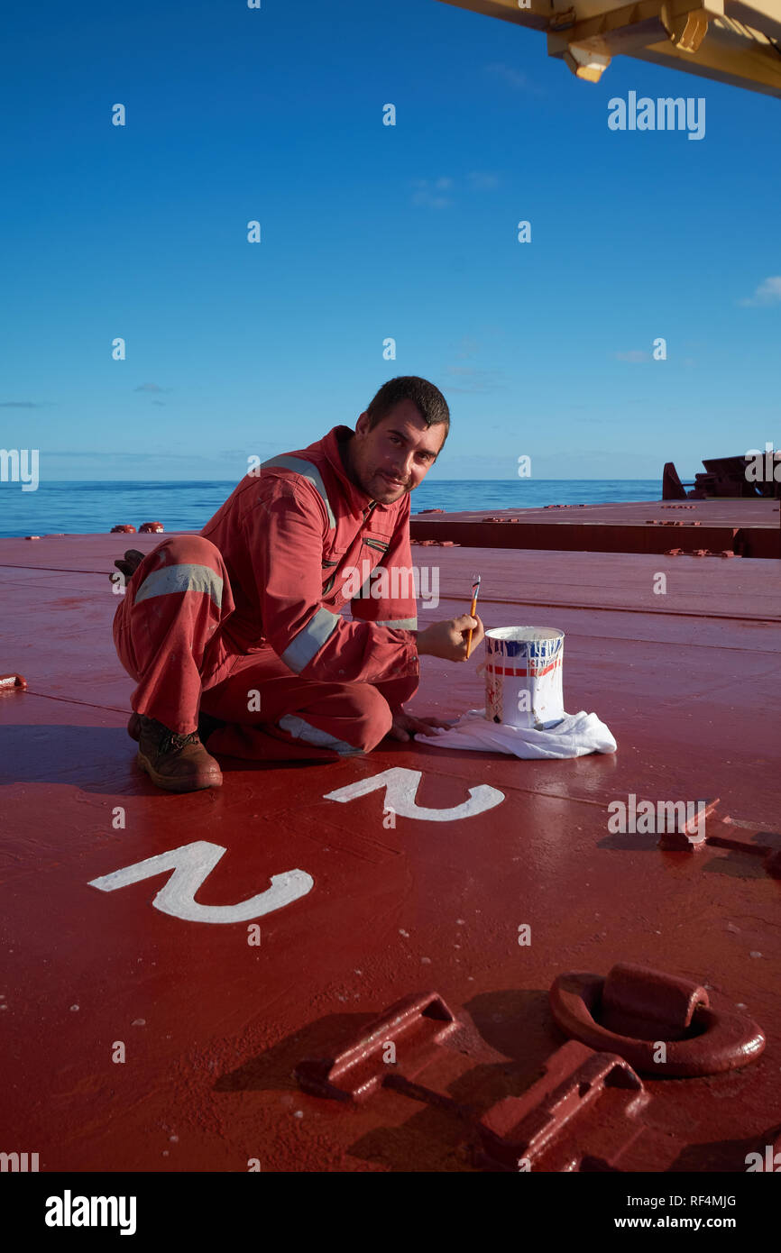 Ships crew members painting hatch cover outdoors with bright blue sky ...