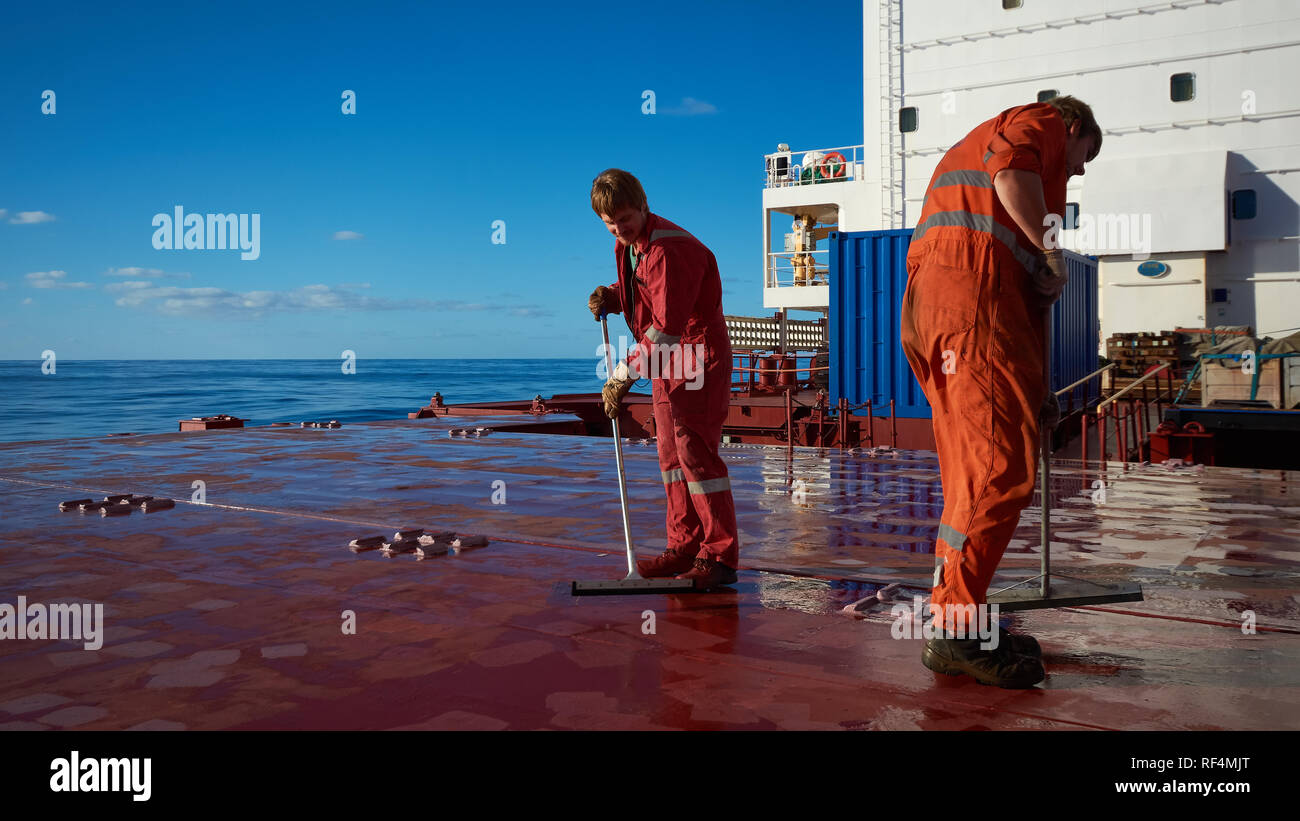 Ships crew members painting hatch cover outdoors with bright blue sky ...