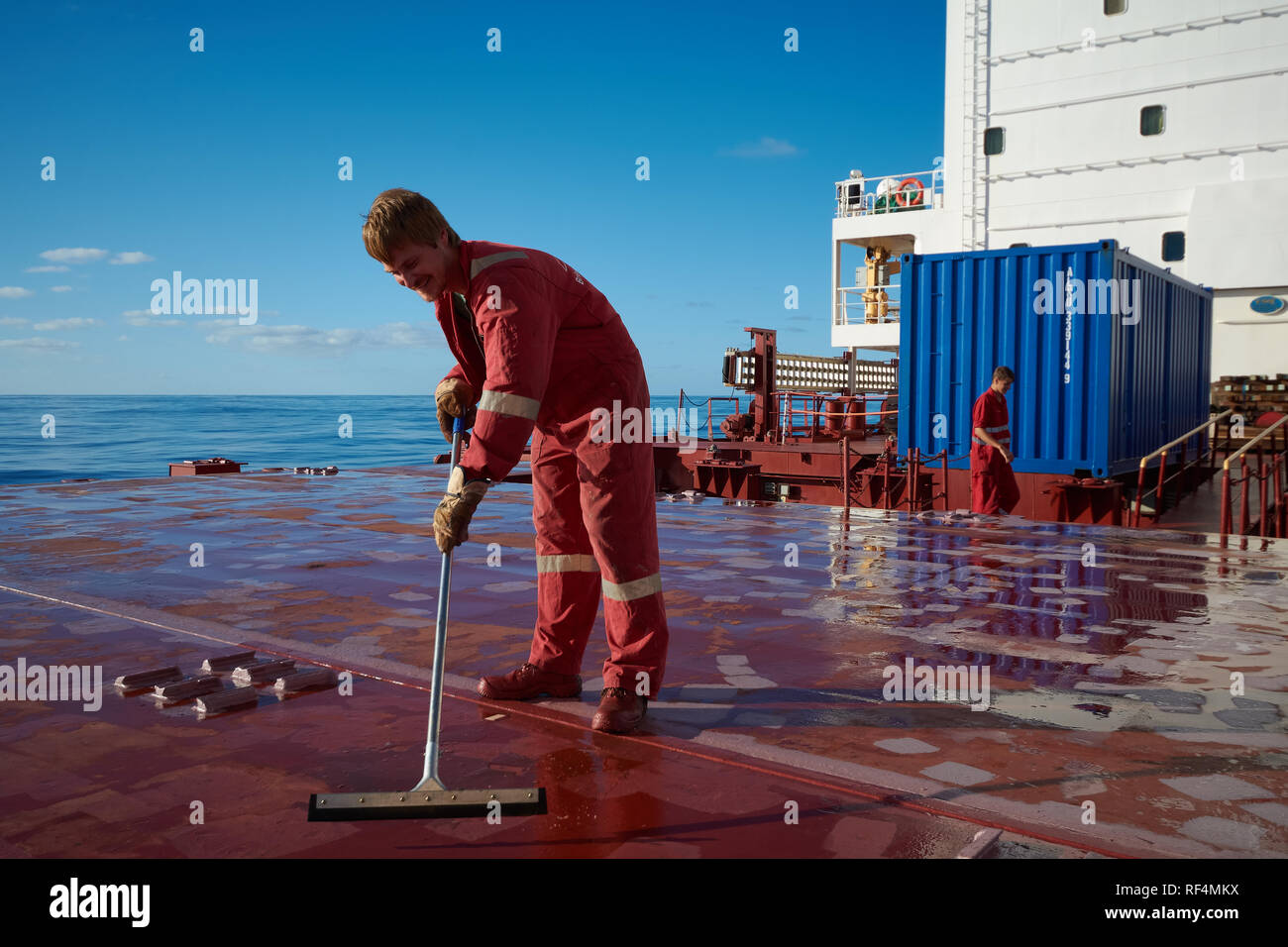 Ships crew members painting hatch cover outdoors with bright blue sky ...