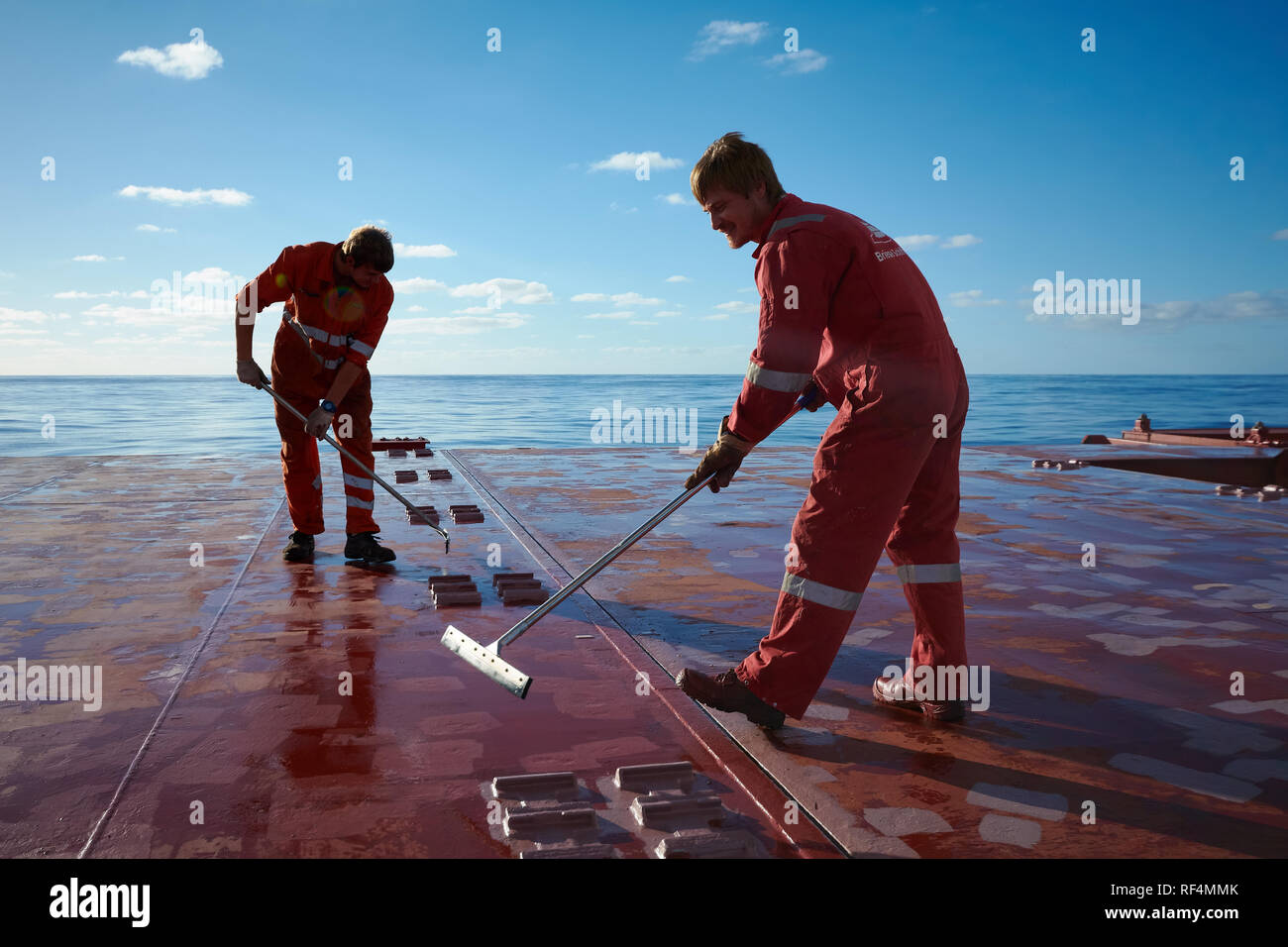 Ships crew members painting hatch cover outdoors with bright blue sky ...