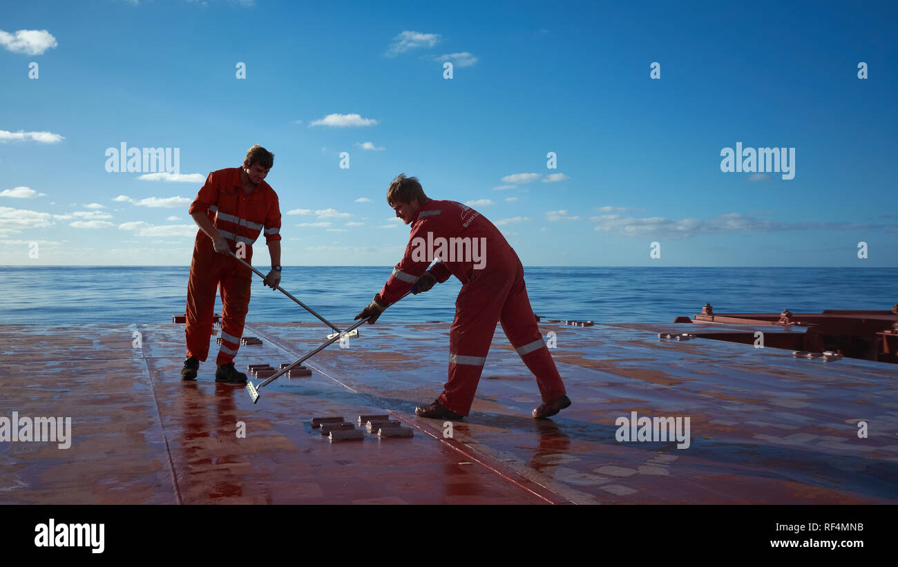 Ships crew members painting hatch cover outdoors with bright blue sky ...