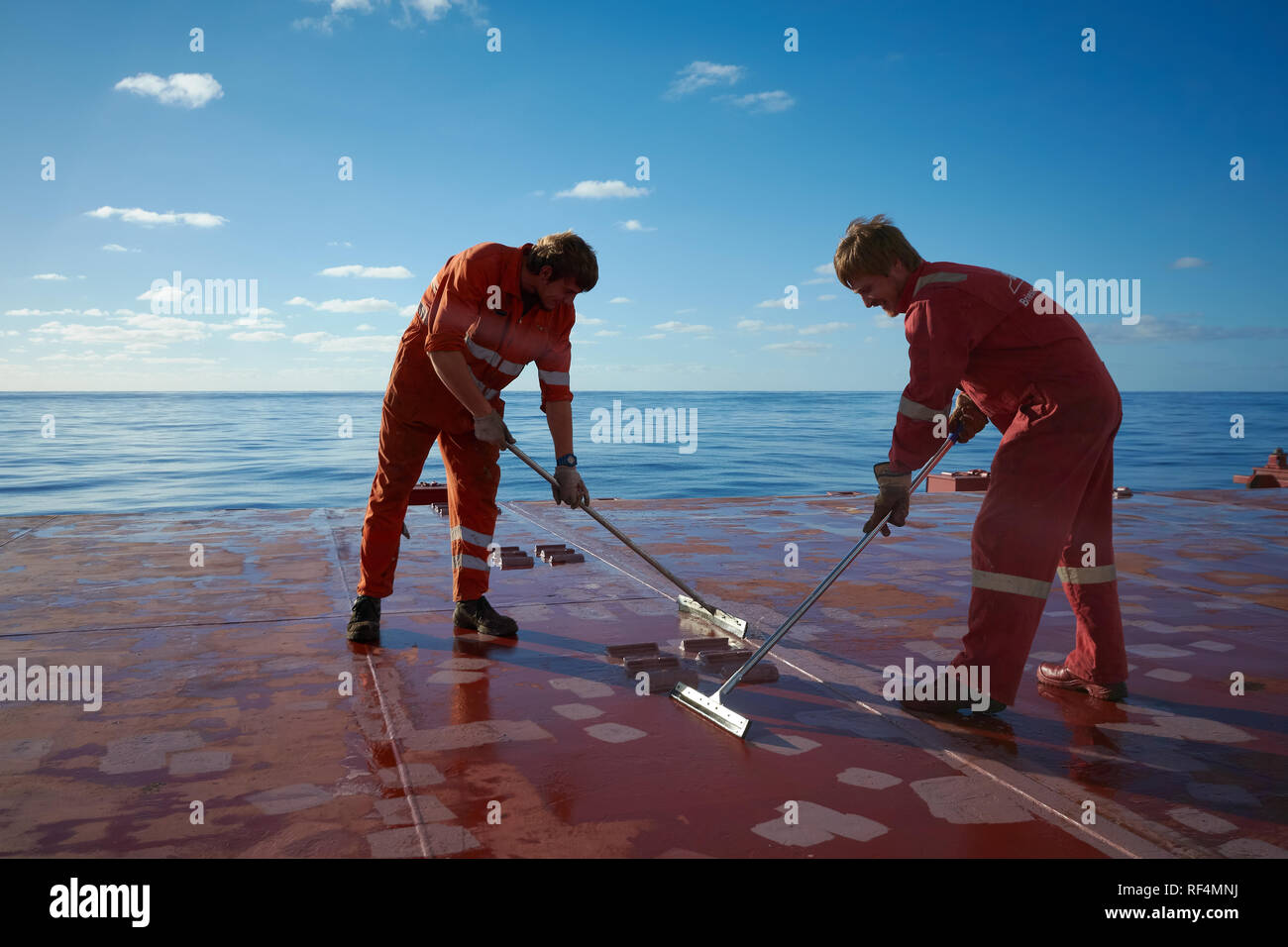 Ships crew members painting hatch cover outdoors with bright blue sky ...