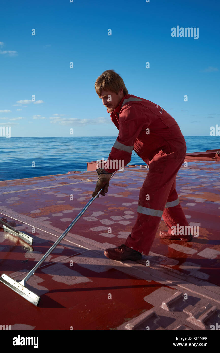 Ships crew members painting hatch cover outdoors with bright blue sky ...