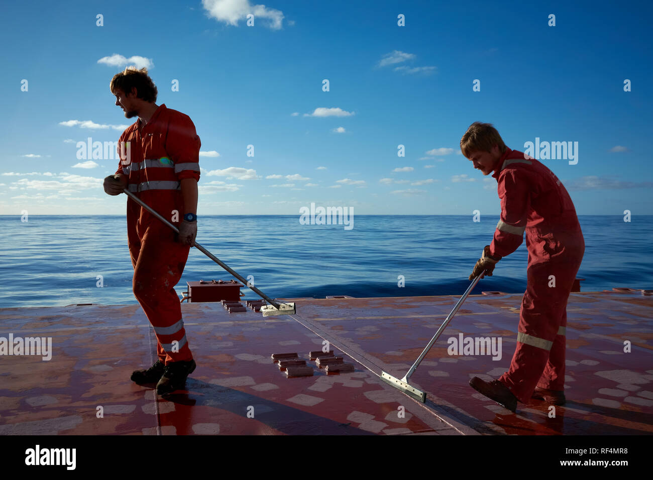 Ships crew members painting hatch cover outdoors with bright blue sky ...