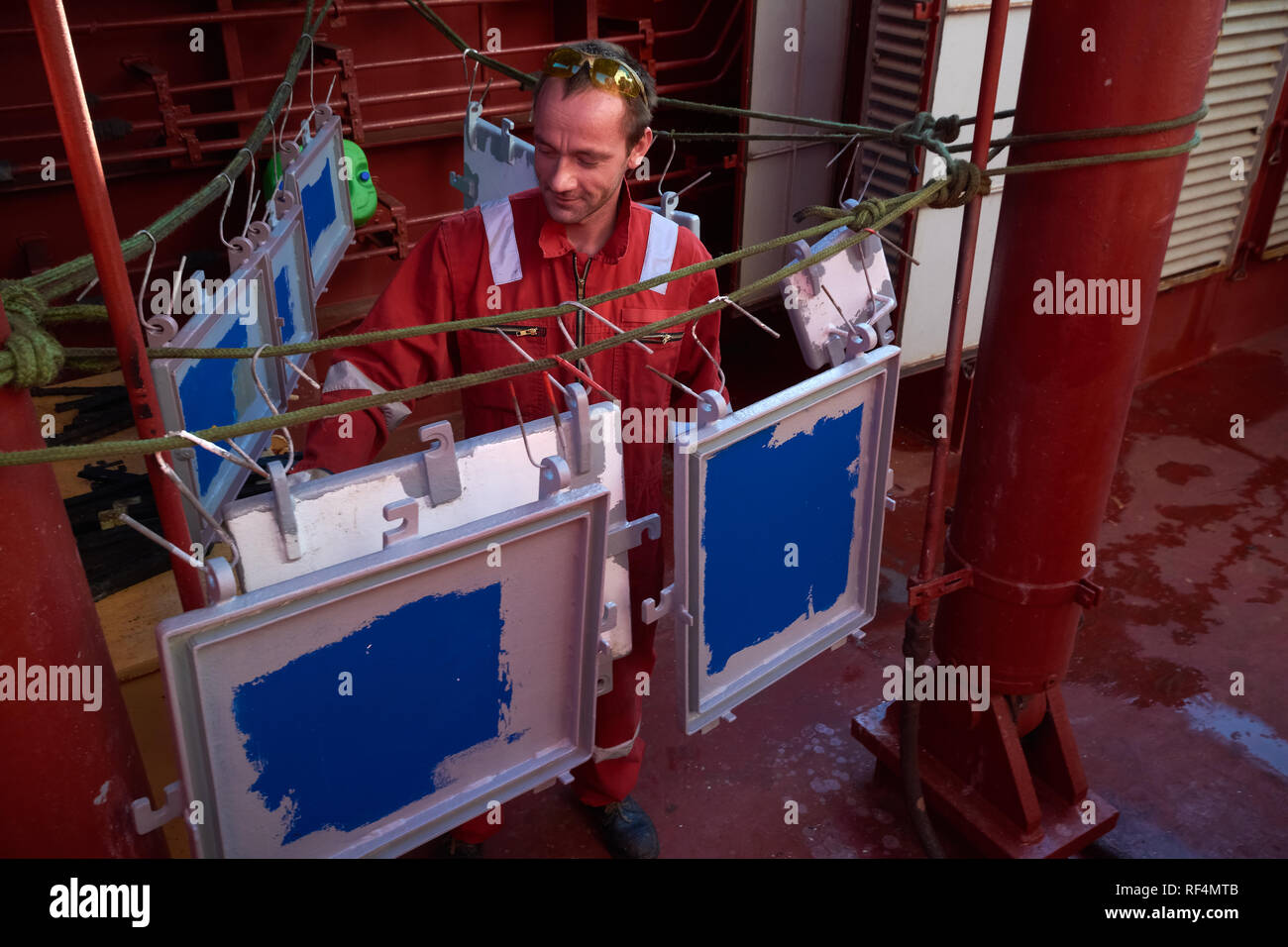 Ships crew members painting hatch cover outdoors with bright blue sky ...