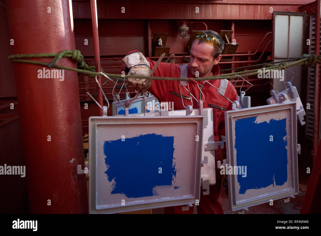 Ships crew members painting hatch cover outdoors with bright blue sky ...