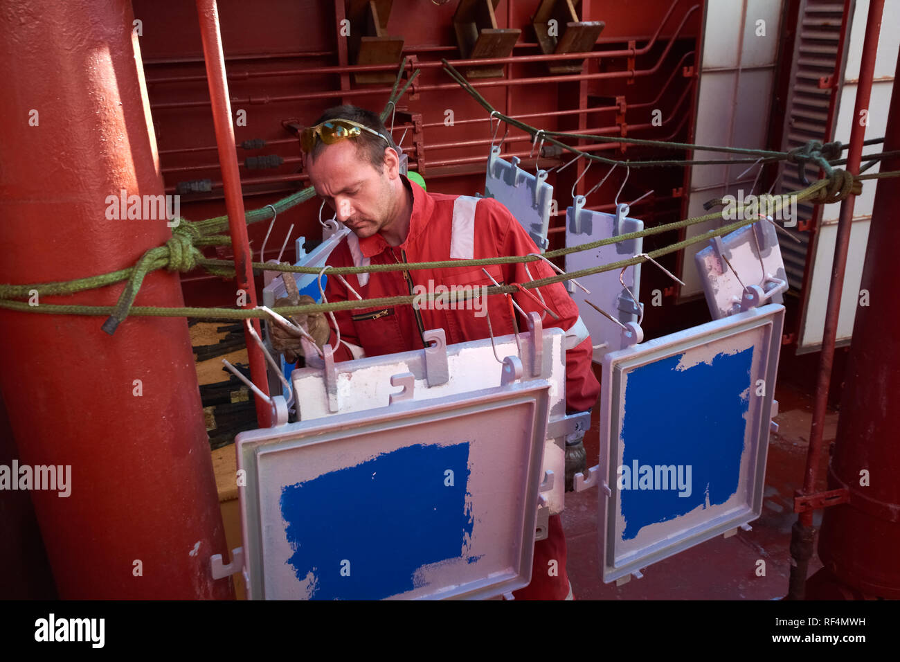 Ships crew members painting hatch cover outdoors with bright blue sky ...