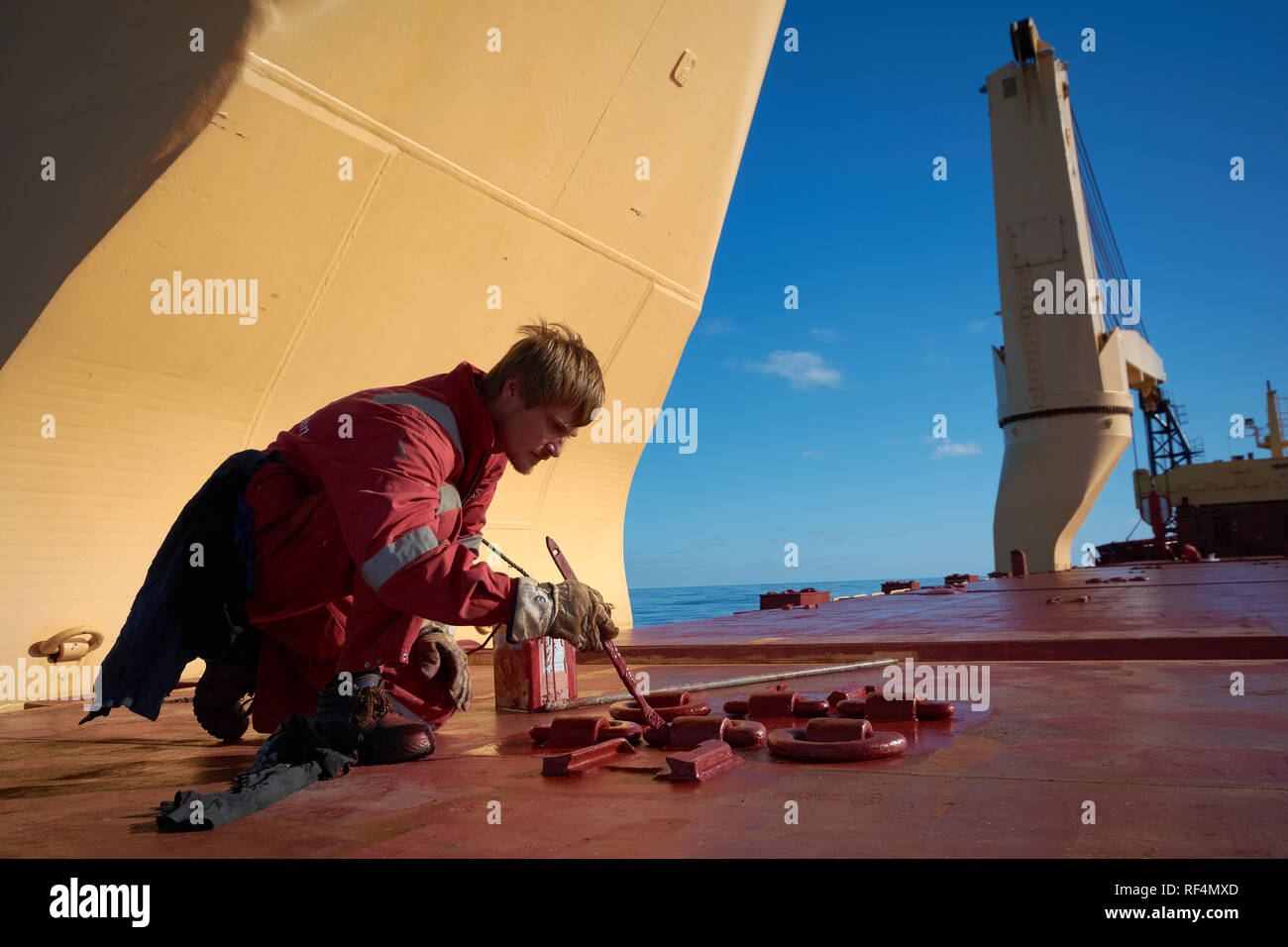 Ships crew members painting hatch cover outdoors with bright blue sky ...